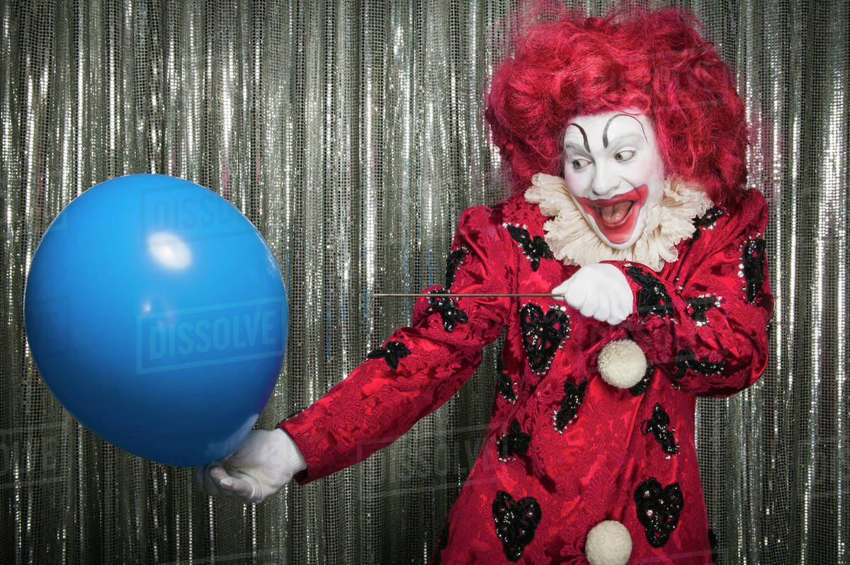 A clown getting ready to pop a balloon with a needle - Royalty-free ...