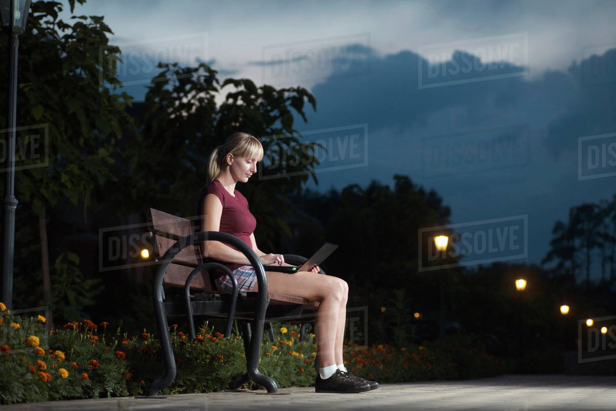 Young woman sitting on park bench and using laptop - Royalty-free Stock ...