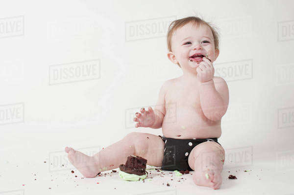 Full length of cute baby boy eating cupcake against white background ...