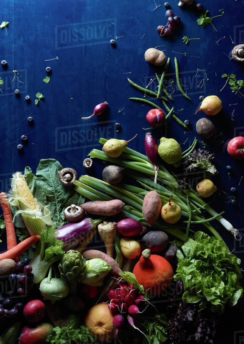 High angle view of fresh vegetables and fruits scattered on blue table ...