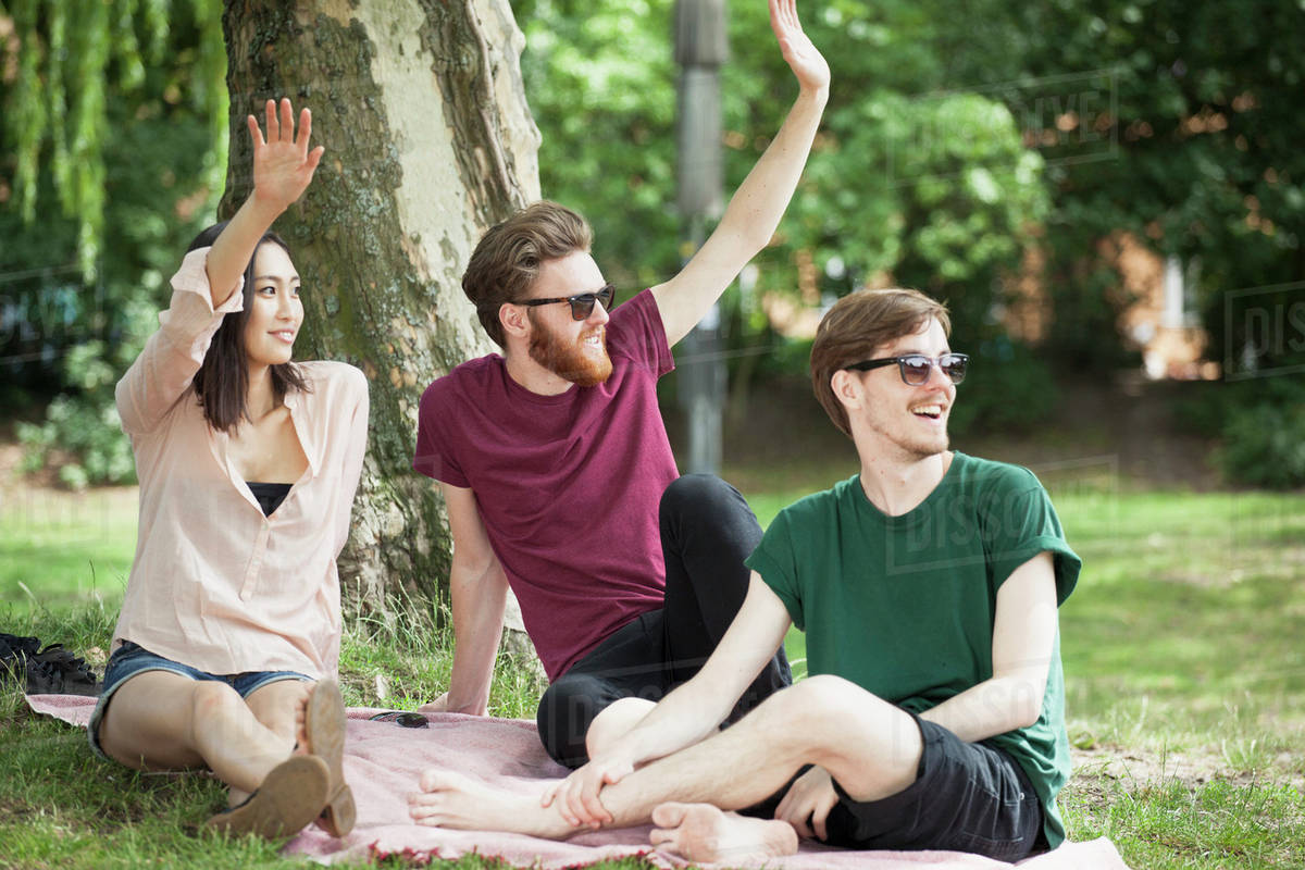 Happy friends waving while relaxing at park - Royalty-free Stock Photo ...