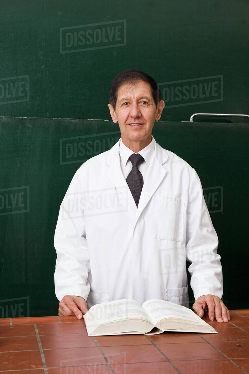 Portrait of a science teacher with an open textbook in his classroom ...