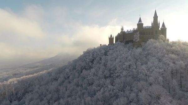 Crane shot of castle on top of mountain surrounded by snow covered ...
