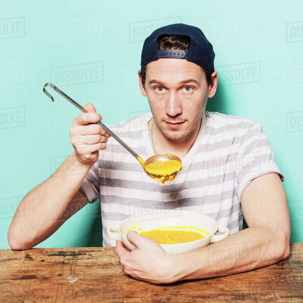 Portrait of confident man having pumpkin soup at table against blue ...