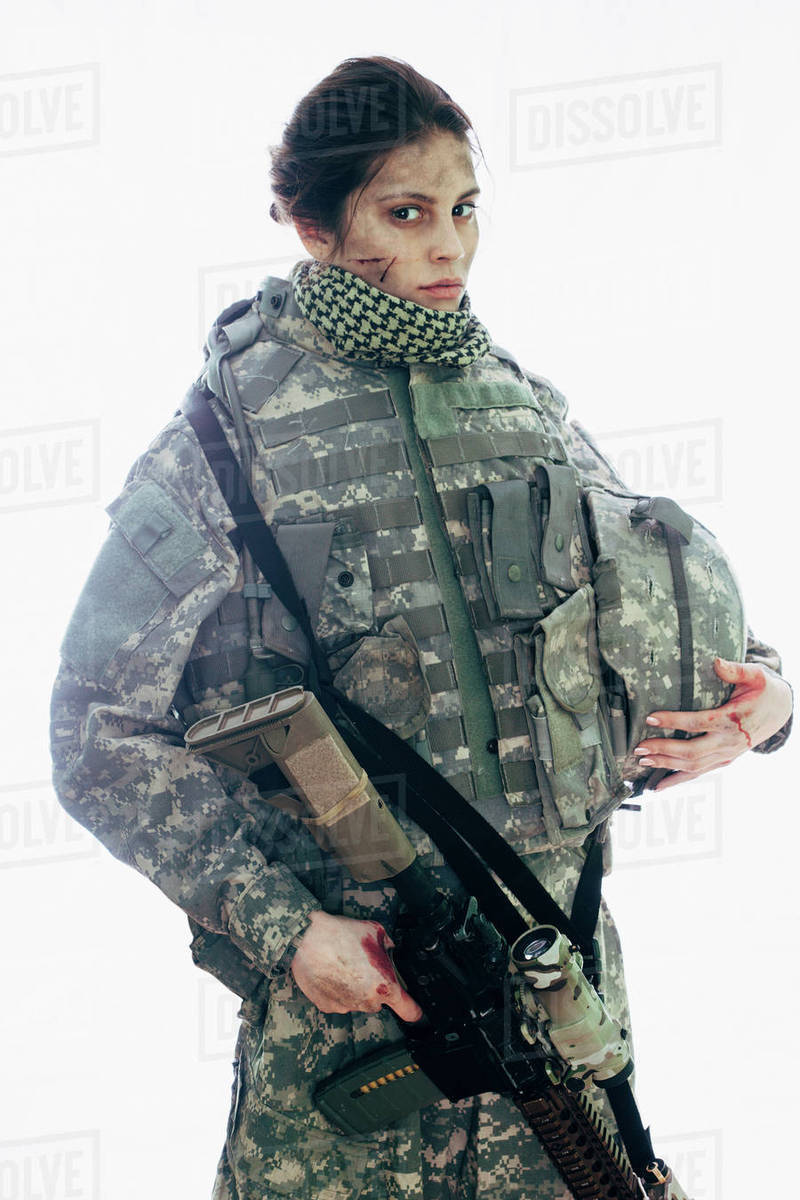 Serious soldier holding rifle and helmet standing against white ...