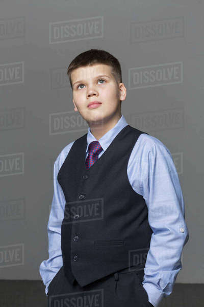 Confident boy looking up while standing against gray background ...