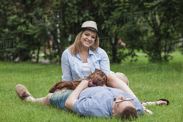 A man napping with his dog lying on him while his girlfriend relaxes by ...