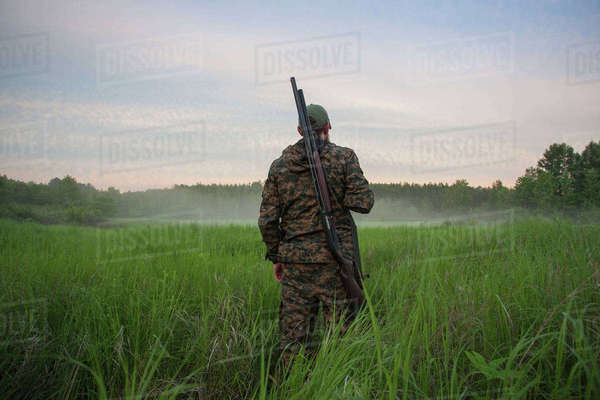 Rear view of hunter standing at grassy field - Royalty-free Stock Photo ...
