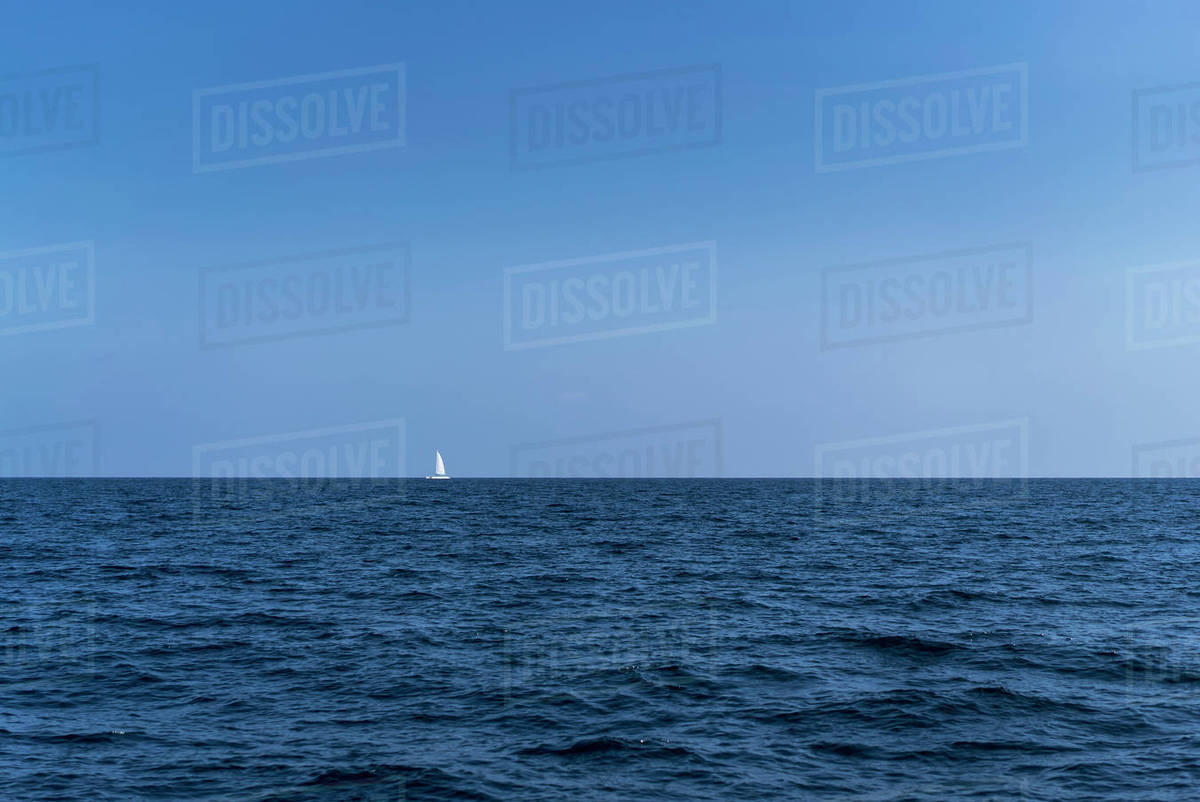 Distant view of sailboat on sea against clear blue sky - Stock Photo ...