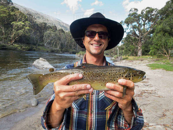 Portrait of happy mature man holding fish by river, Jindabyne, New ...