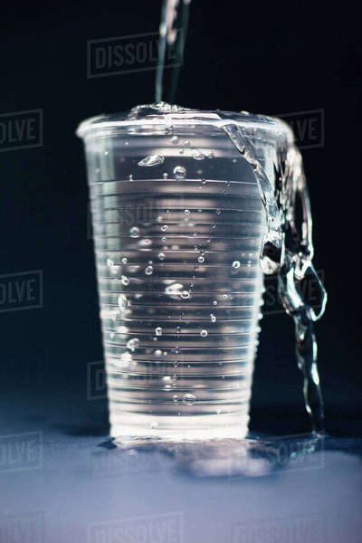 Close-up of water pouring in overflowing glass on table against black ...