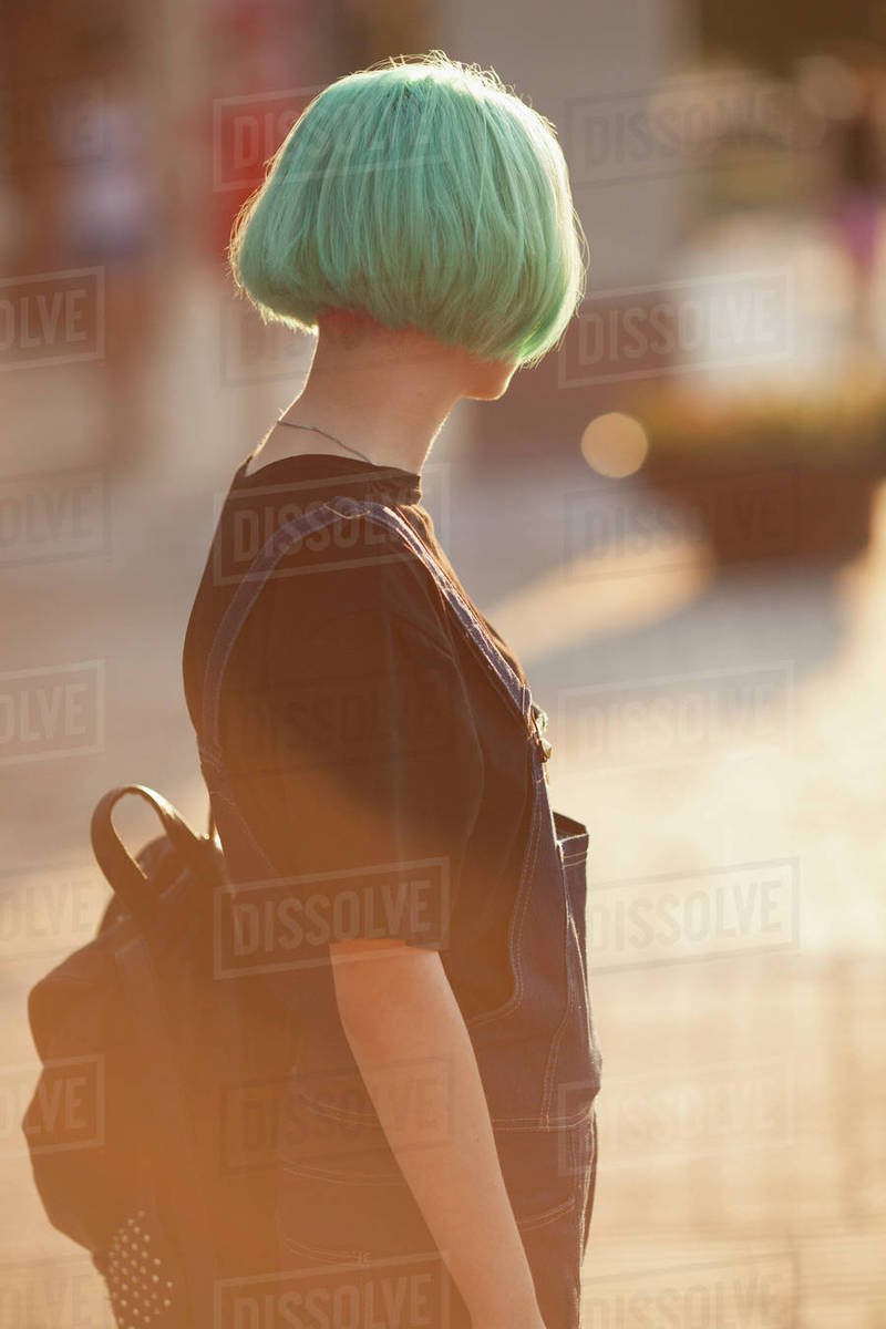 Teenage girl carrying backpack while standing in city during sunny day ...