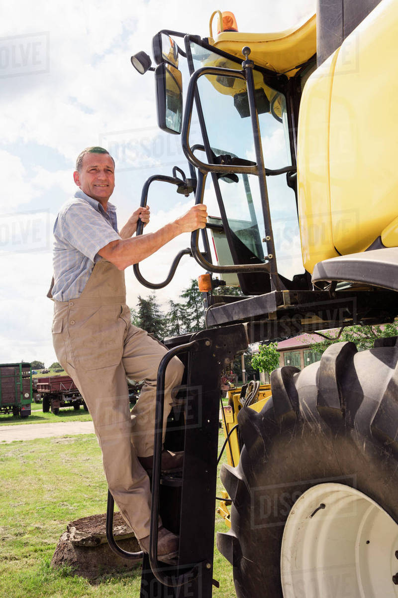 Full length of man climbing on agricultural machinery at farm against ...