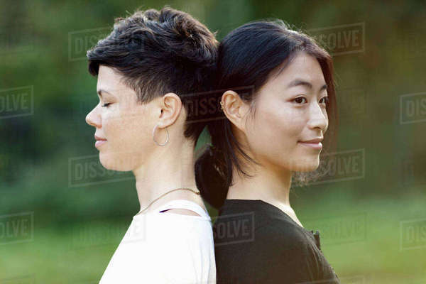 Close-up side view of friends standing back to back at park - Royalty ...