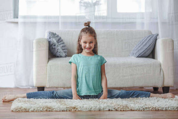 Full length portrait of smiling girl doing splits on rug in living room ...