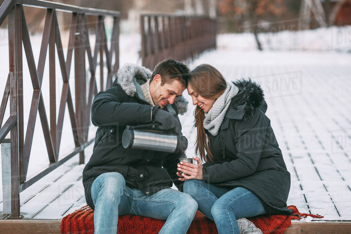 Happy man pouring drink from insulated container on boardwalk during ...