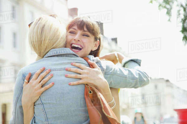 Happy young women friends hugging on sunny urban sidewalk - Royalty ...