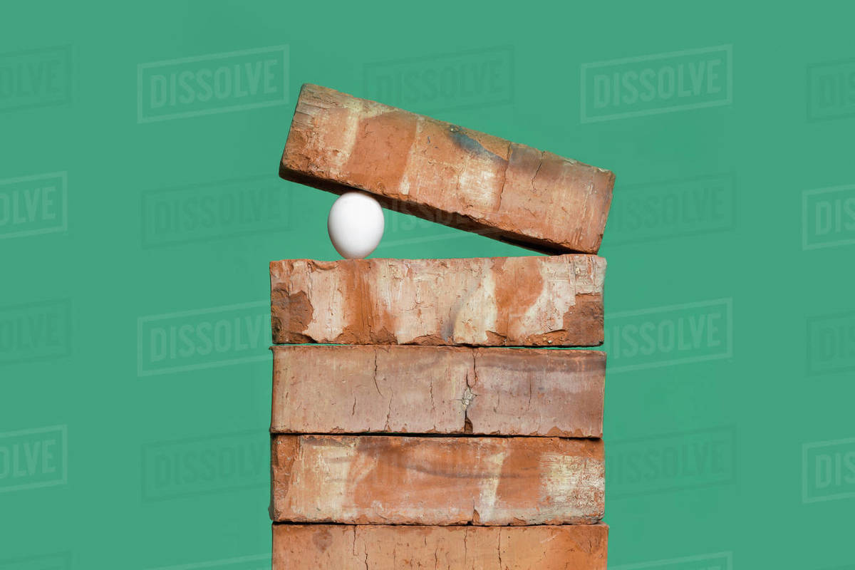 Egg between bricks on green background - Stock Photo - Dissolve