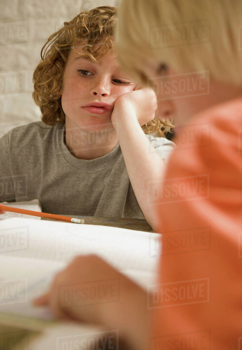 Two young boys writing and sitting in the classroom one of them is ...