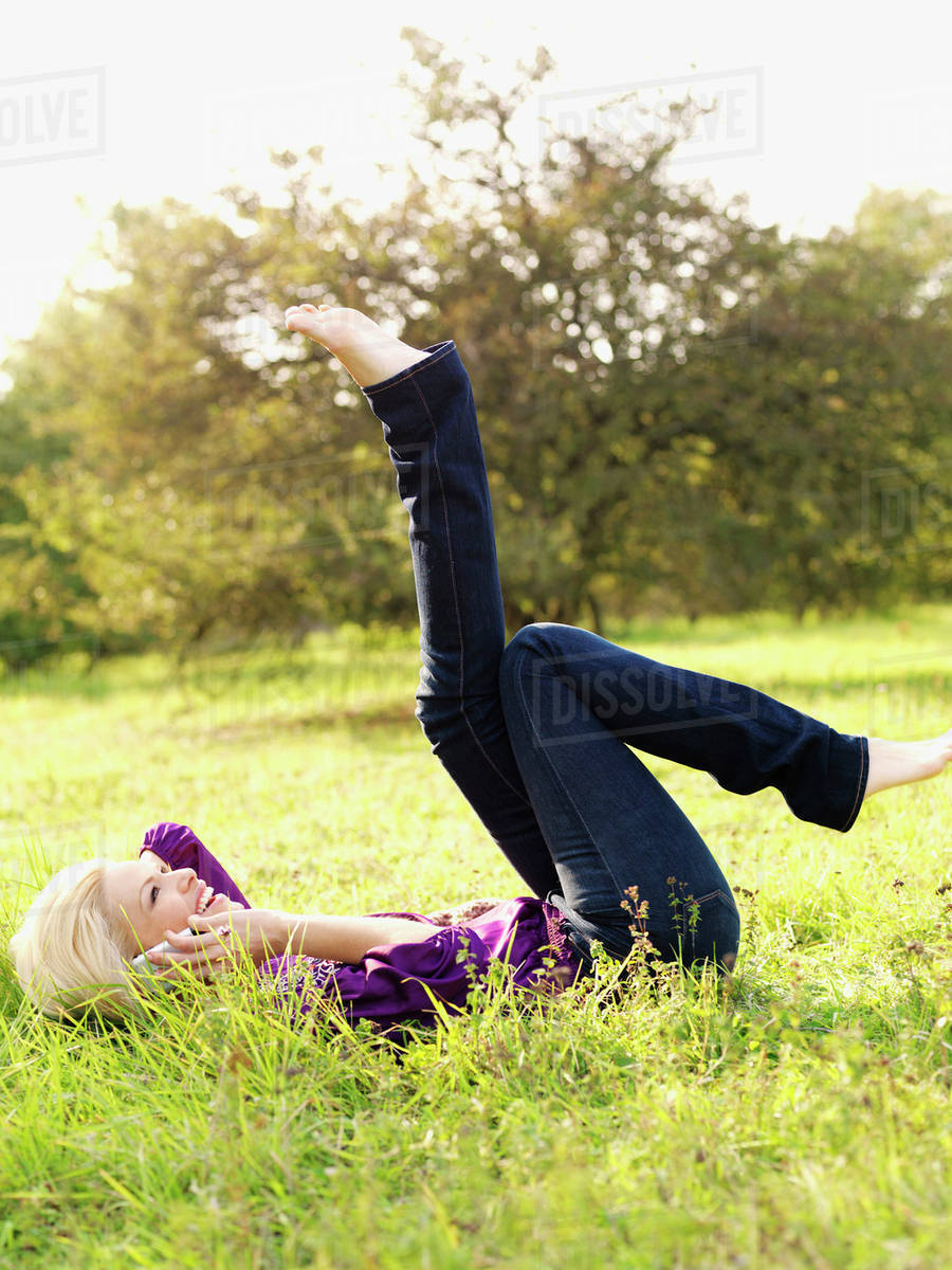 A woman lying on her back with her legs raised using a mobile phone ...